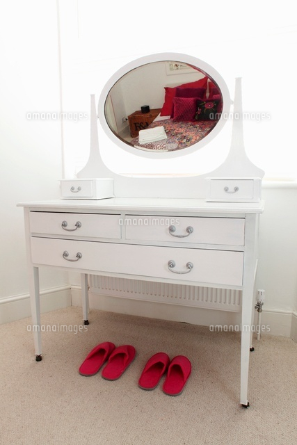 A white make-up table with an oval mirror and two pairs of p ...