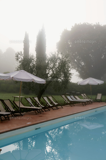 Foggy morning -- poolside with lounge chairs and sun umbrell ...
