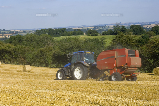 Tractor collecting hay bales at harvest time, seen from the Cotswolds ...