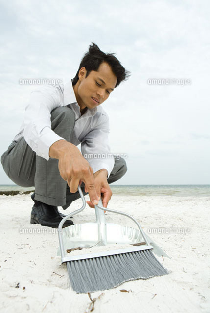 Man sweeping sand into dustpan[11001035834]の写真素材・イラスト素材｜アマナイメージズ