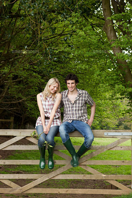 Young couple sitting on gate[11015198999]の写真素材・イラスト素材｜アマナイメージズ