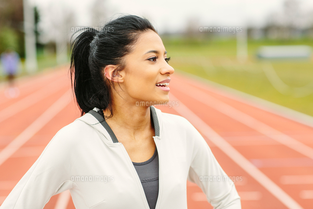 Portrait of young girl on running track, looking away, smiling ...
