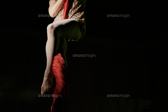 Waist down view of young female aerial acrobat wrapped around silk rope ...