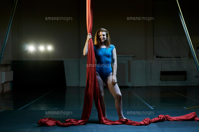 Portrait of young female aerial acrobat holding red silk rope ...