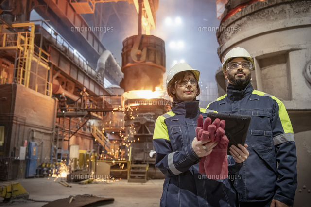 Male and female steelworkers using digital tablet during steel pour in ...