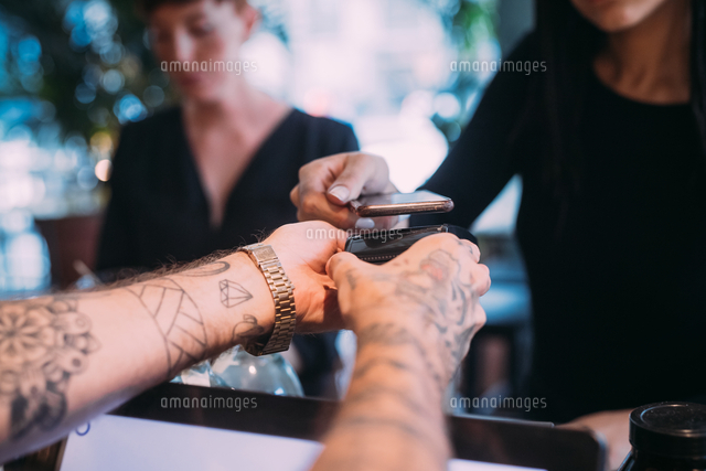 Close up of tattooed bartender standing at counter, handing card reader ...
