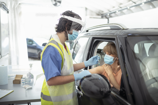 Young male nurse in hi-vis vaccinating older woman in car in drive-in ...