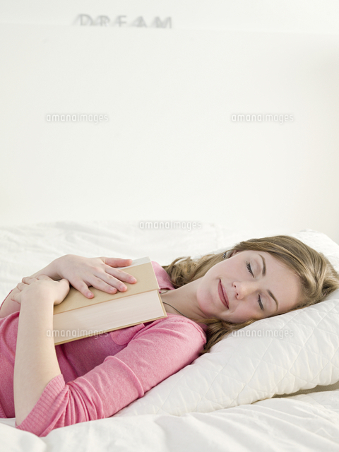 Caucasian woman napping with book on bed[11018056553]の写真素材・イラスト素材｜アマナイメージズ