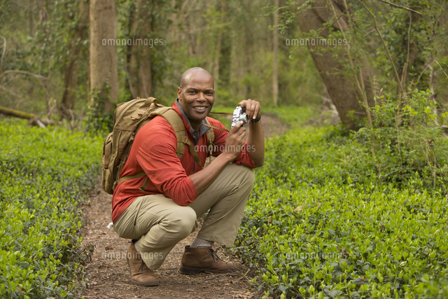 African American man crouching on path in forest holding camera ...