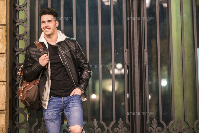 Smiling Caucasian man carrying bag leaning on gate[11018096315]の写真素材 ...