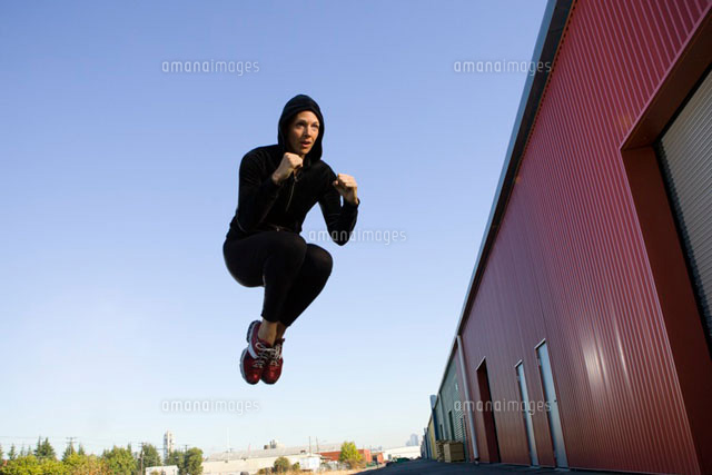Female athlete jumping near warehouse[11029007265]の写真素材・イラスト素材｜アマナイメージズ