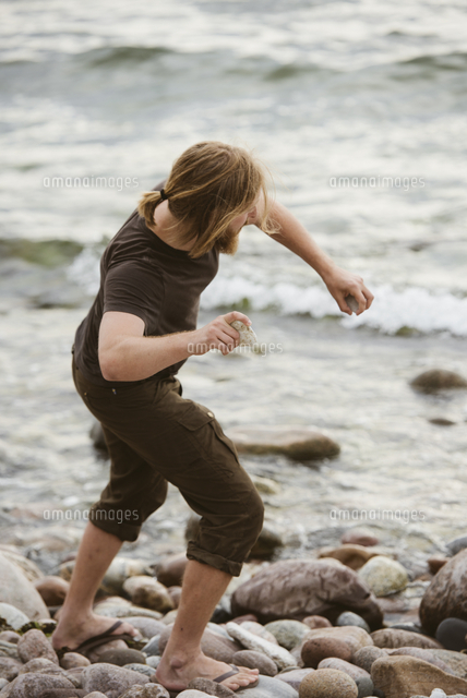 Young man throwing stones on beach[11077013301]の写真素材・イラスト素材｜アマナイメージズ