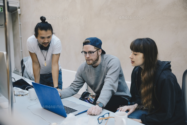 Multi-ethnic male and female computer programmers using laptop at desk ...
