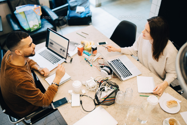 High angle view of male and female programmers discussing while sitting at desk in creative ...