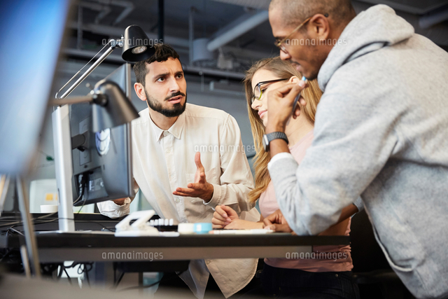 Creative businessman explaining colleagues over computer at desk in ...