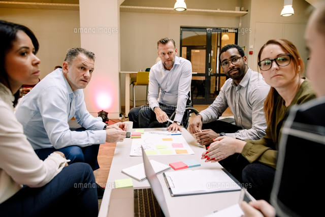 Sales executives looking at businesswoman during meeting in office ...