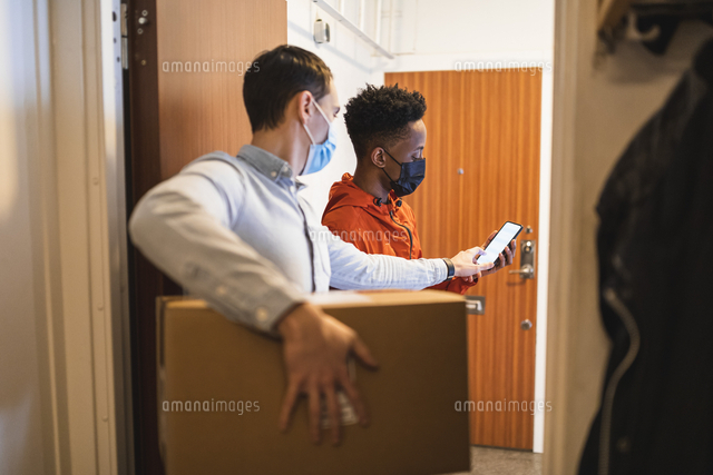 Male customer receiving parcel from young delivery man during COVID-19 ...