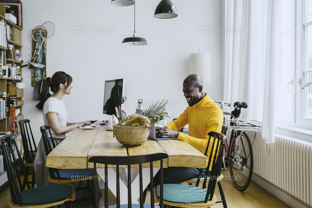Smiling male and female freelancer sitting at table working from home ...
