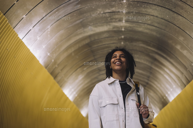 Happy young non-binary person with backpack standing in illuminated ...