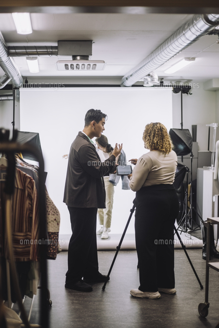 Side view of male fashion designer assisting photographer during photo ...