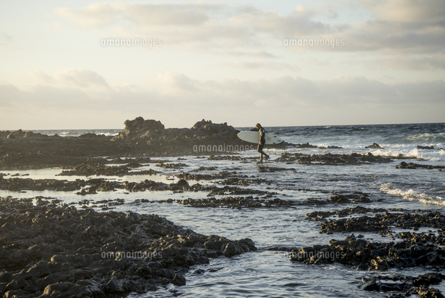 A man in a wetsuit preparing to surf at Corralejo in Fuerteventura ...