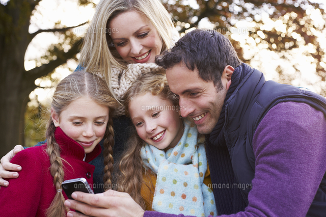 Family using cell phone outdoors[11086002512]の写真素材・イラスト素材｜アマナイメージズ