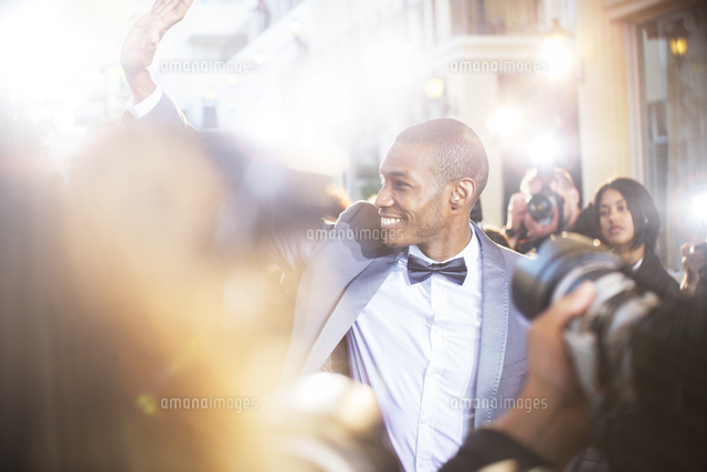 Smiling celebrity waving to paparazzi photographers at event ...