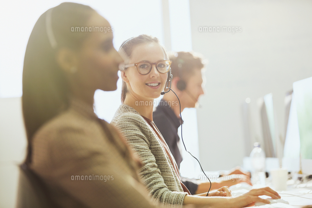 Portrait smiling female telemarketer wearing headset at computer in ...