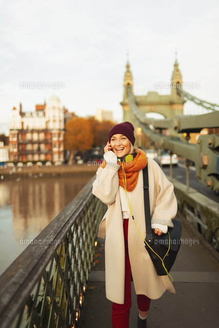 Young woman in stocking cap and scarf talking on smart phone on urban ...