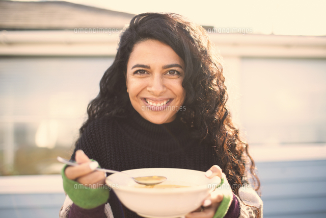 Portrait beautiful happy woman eating chowder on sunny patio ...