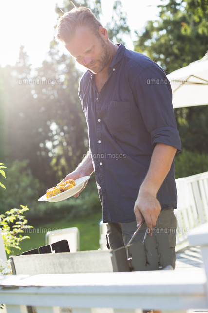Sweden, Stockholm Archipelago, Grasko, Man preparing grilled corn ...