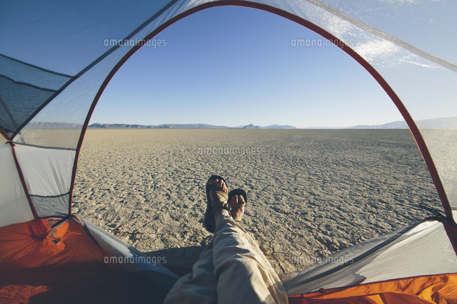 Man reclining in camping tent, expansive desert and playa in distance ...