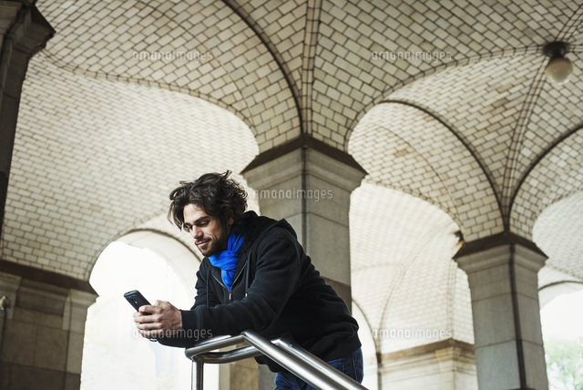 A man checking his smart phone and leaning on a stair railing ...