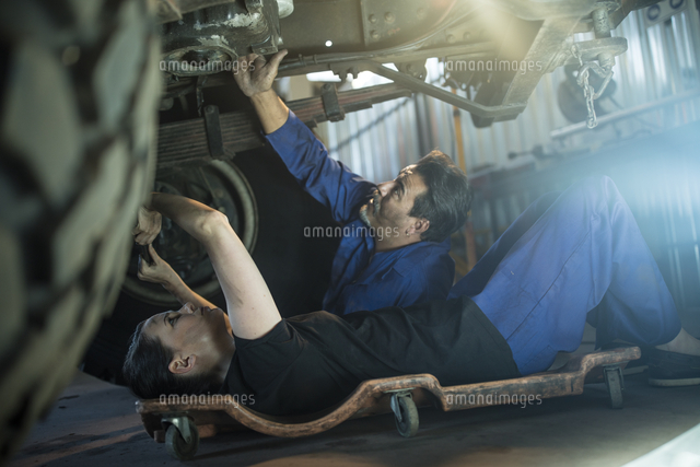 Mechanics working at fire brigade workshop, lying on creeper ...
