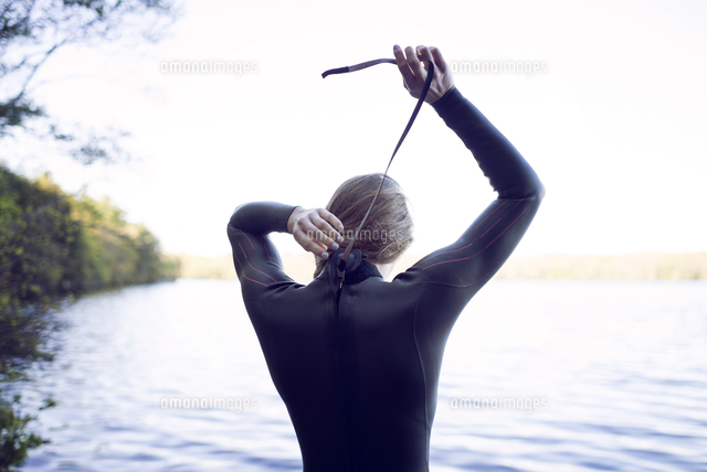 Rear view of female swimmer wearing wetsuit at lakeshore[11100035895]の ...