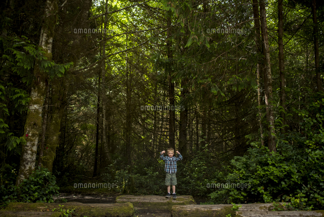 Portrait of boy flexing muscles while standing on log in forest ...