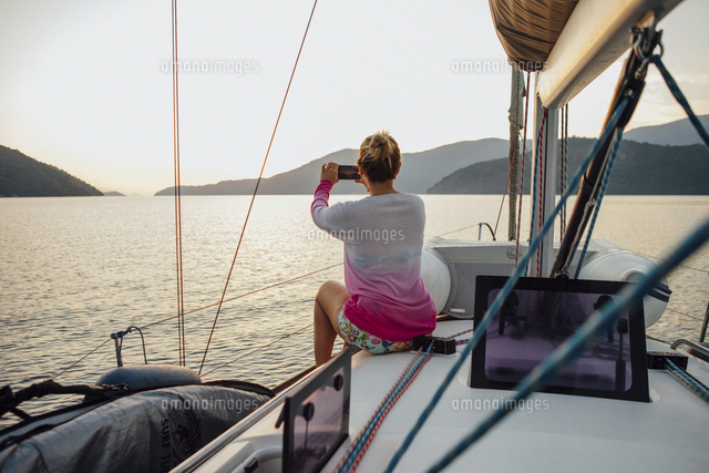Rear view of woman photographing while traveling in sailboat on sea ...