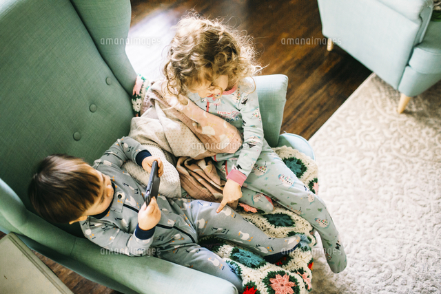High angle view of siblings sitting on chair at home[11100080367]の写真素材 ...