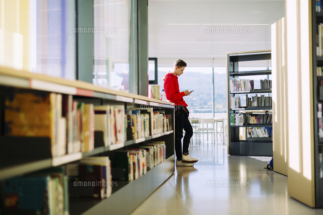 Side view of man using mobile phone while standing in library ...