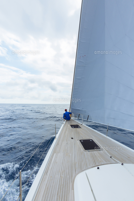 Rear view of man sitting on sailing ship in sea against cloudy sky ...
