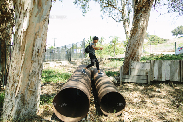 Side view of girl with backpack jumping on pipes against clear sky ...