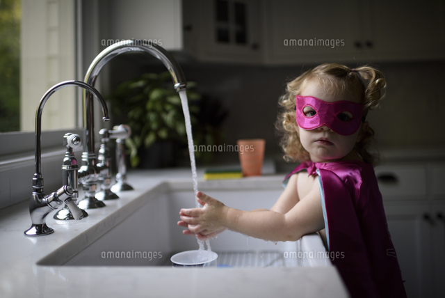 Portrait of girl wearing superhero costume washing hands in kitchen ...