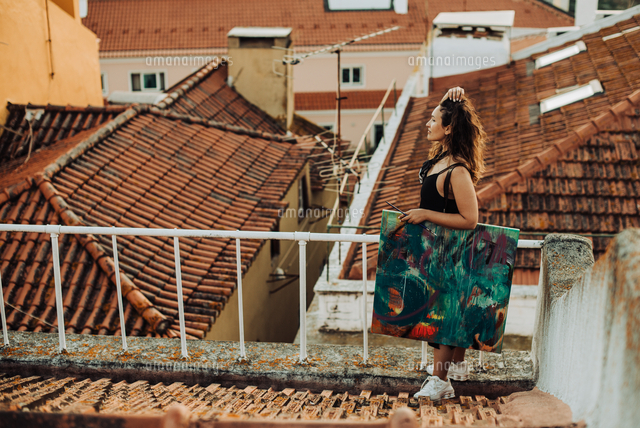 Woman standing holding abstract art painting while standing on roof ...