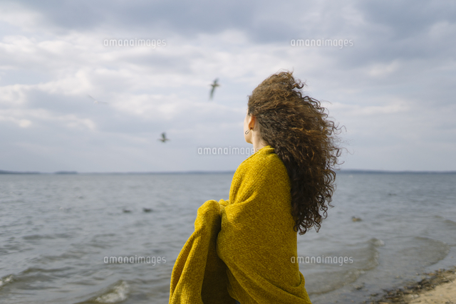 a woman stands on the shore of the lake covered with a yellow cape ...