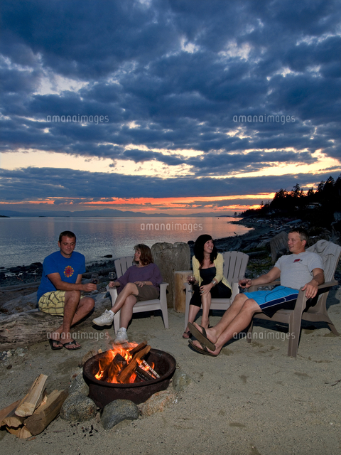 After a beautiful summer day, friends relax around the fire near ...